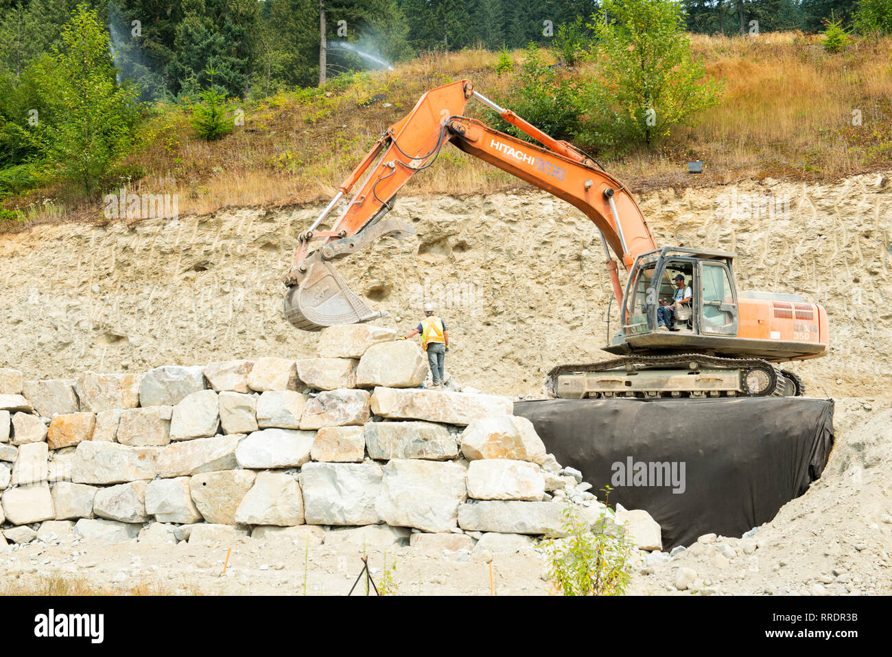 Construction workers assemble a rock wall during landscape preparation ...