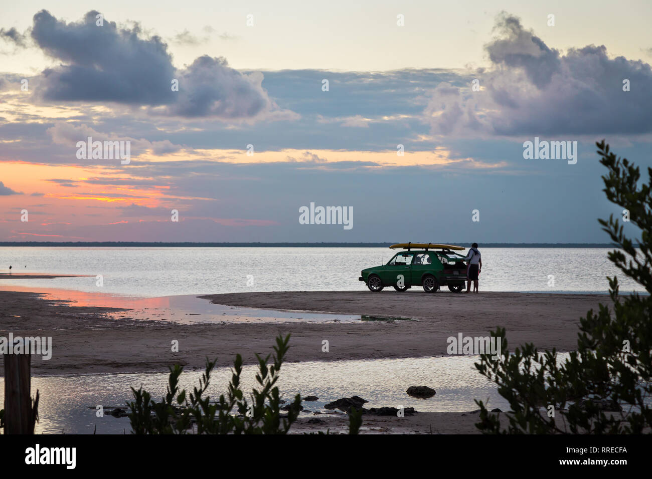 A retro surf car with a surfboard on a sand bar near the ocean with the ...