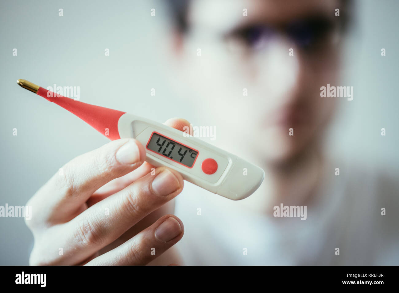 Man holds a red fever thermometer with high temperature in his hand ...