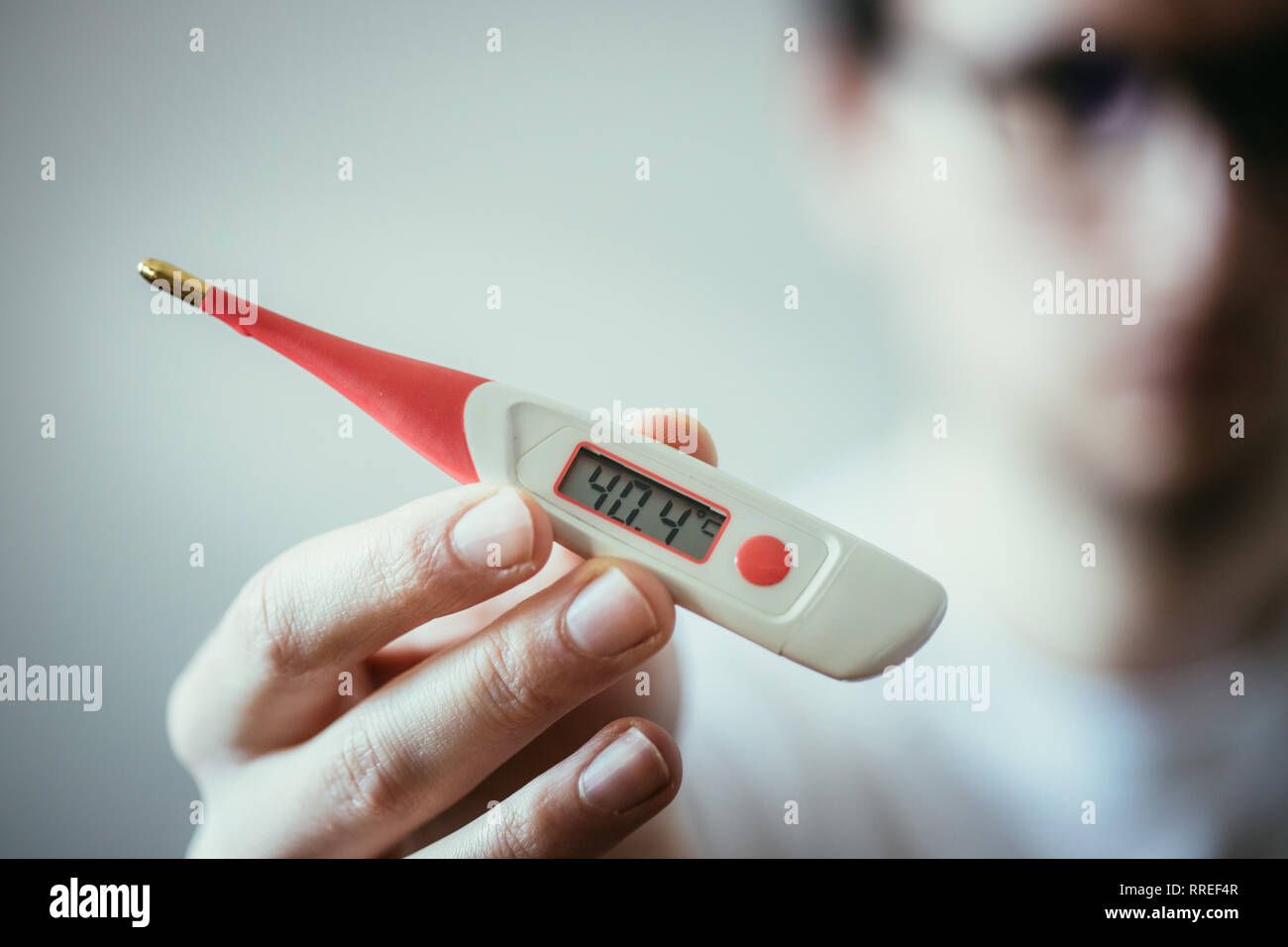 Man holds a red fever thermometer with high temperature in his hand ...