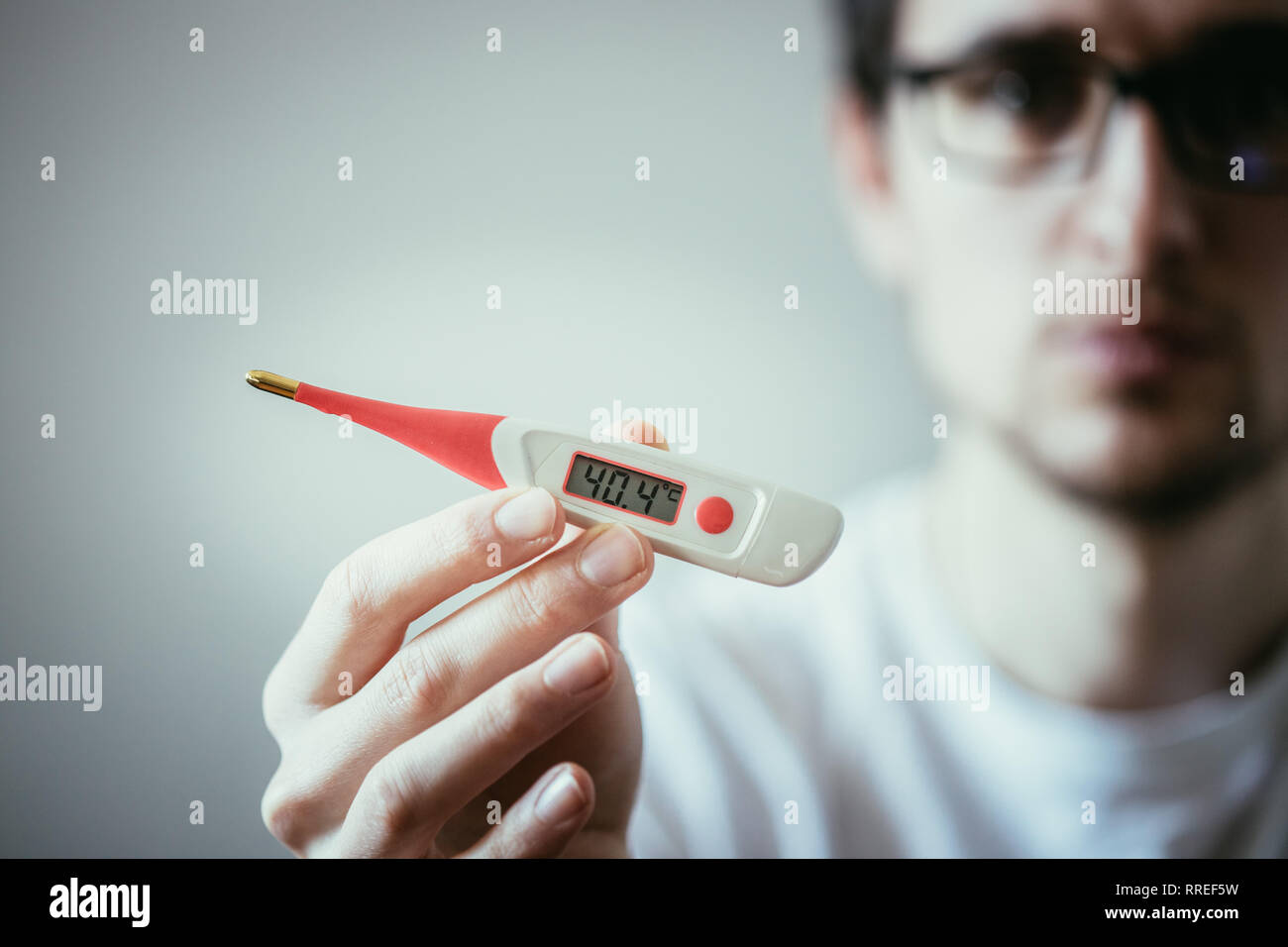 Man holds a red fever thermometer with high temperature in his hand ...