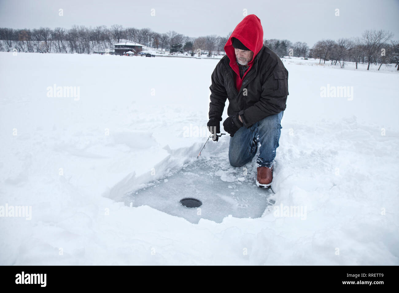 A middle aged man ice fishing on a snowy lake in Minnesota during the ...