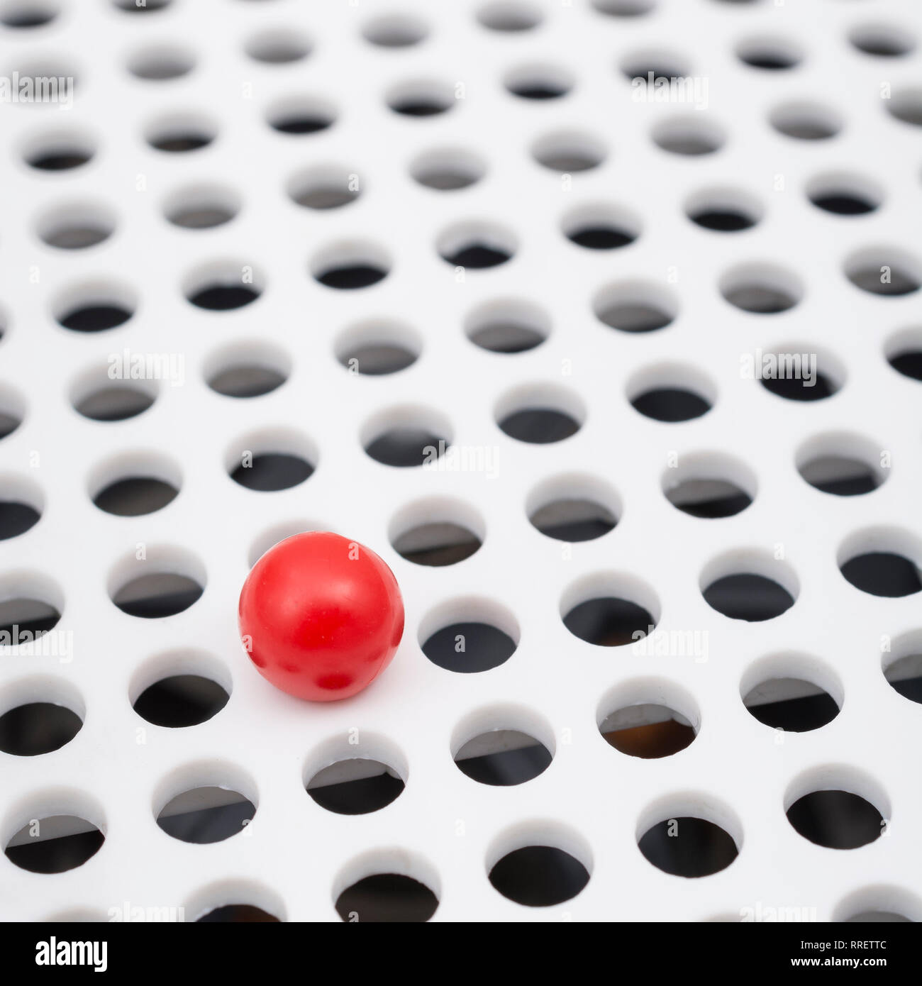 Abstract holes. Small solitary red plastic ball isolated on round holed ...