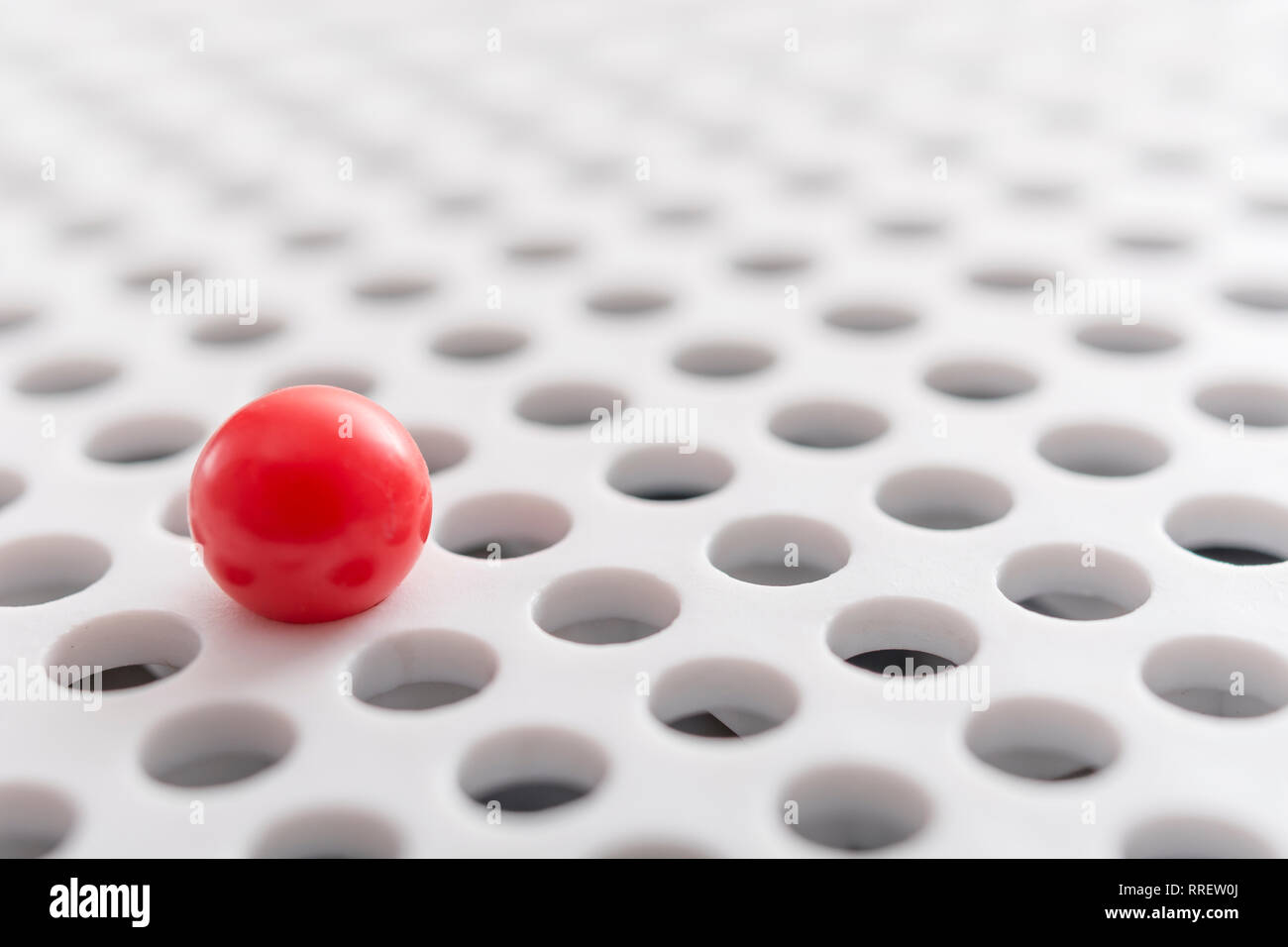 Abstract holes. Small solitary red plastic ball isolated on round holed ...