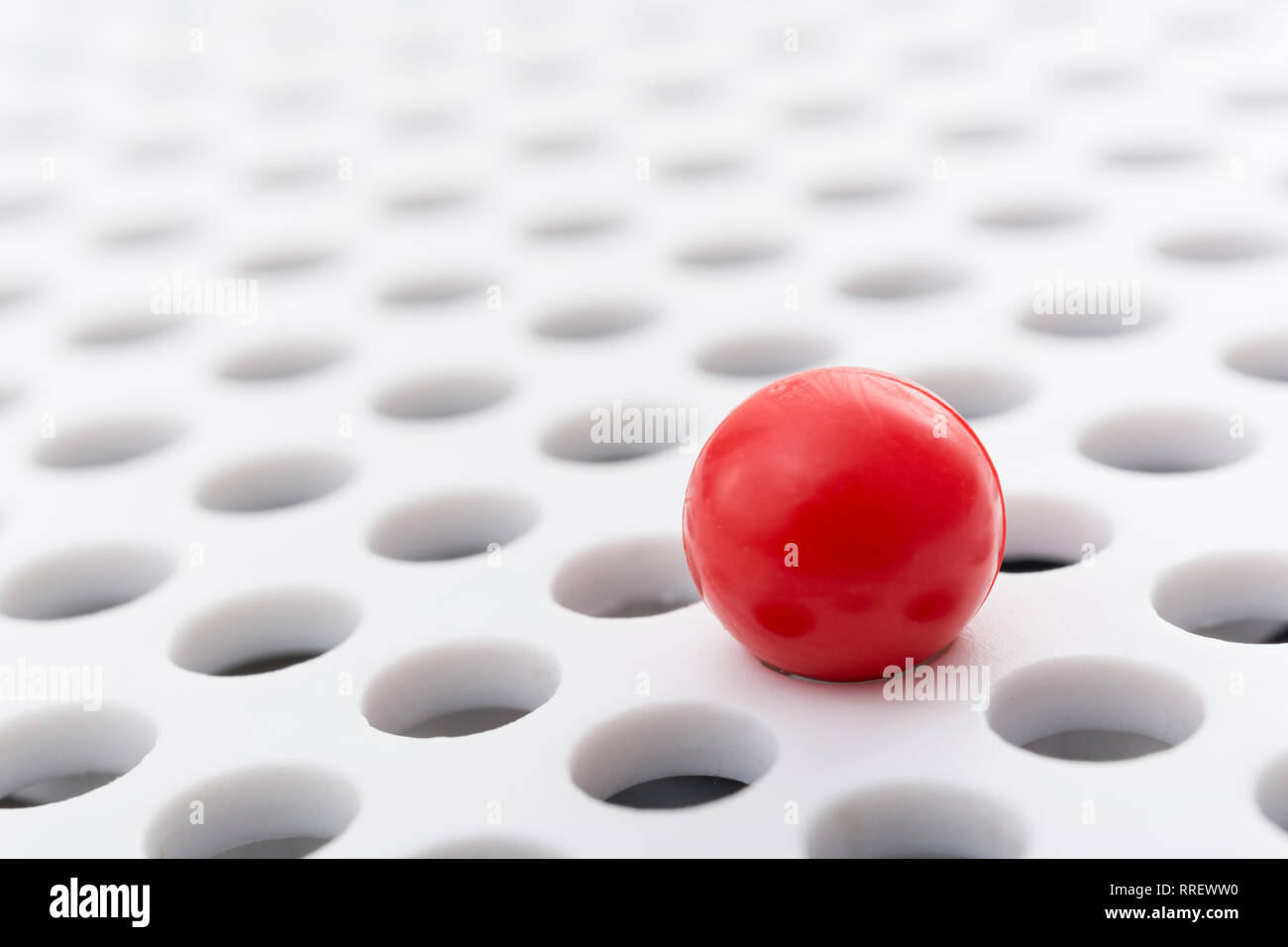 Abstract holes. Small solitary red plastic ball isolated on round holed ...