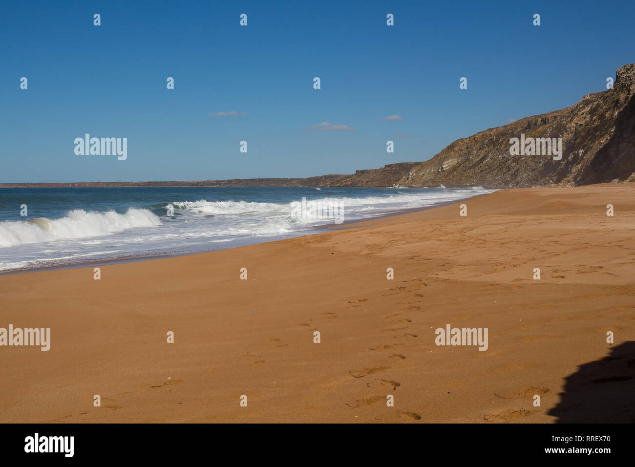 Dark yellow color of the sandy beach, lined by rocky mountain. Waves of ...
