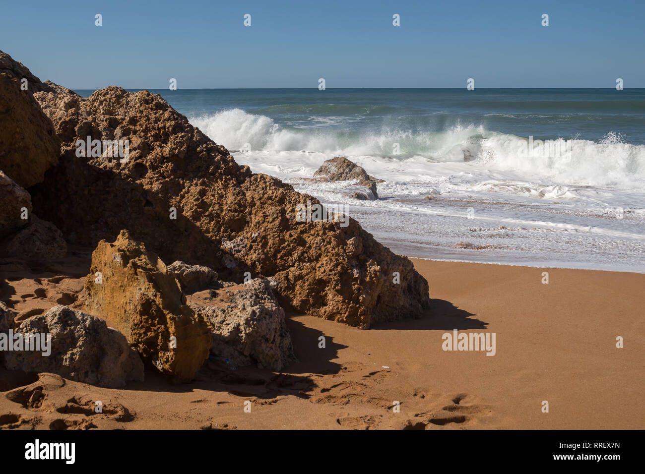 Rocks on the clean beach with dark yellow sand. Foamy waves of the ...