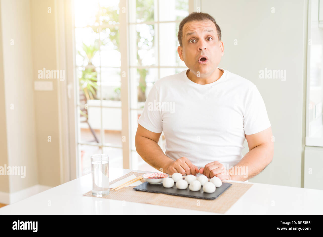 Middle age man eating asian dumplings at home afraid and shocked with ...