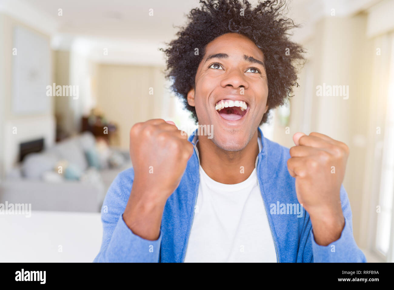African American man at home excited for success with arms raised ...