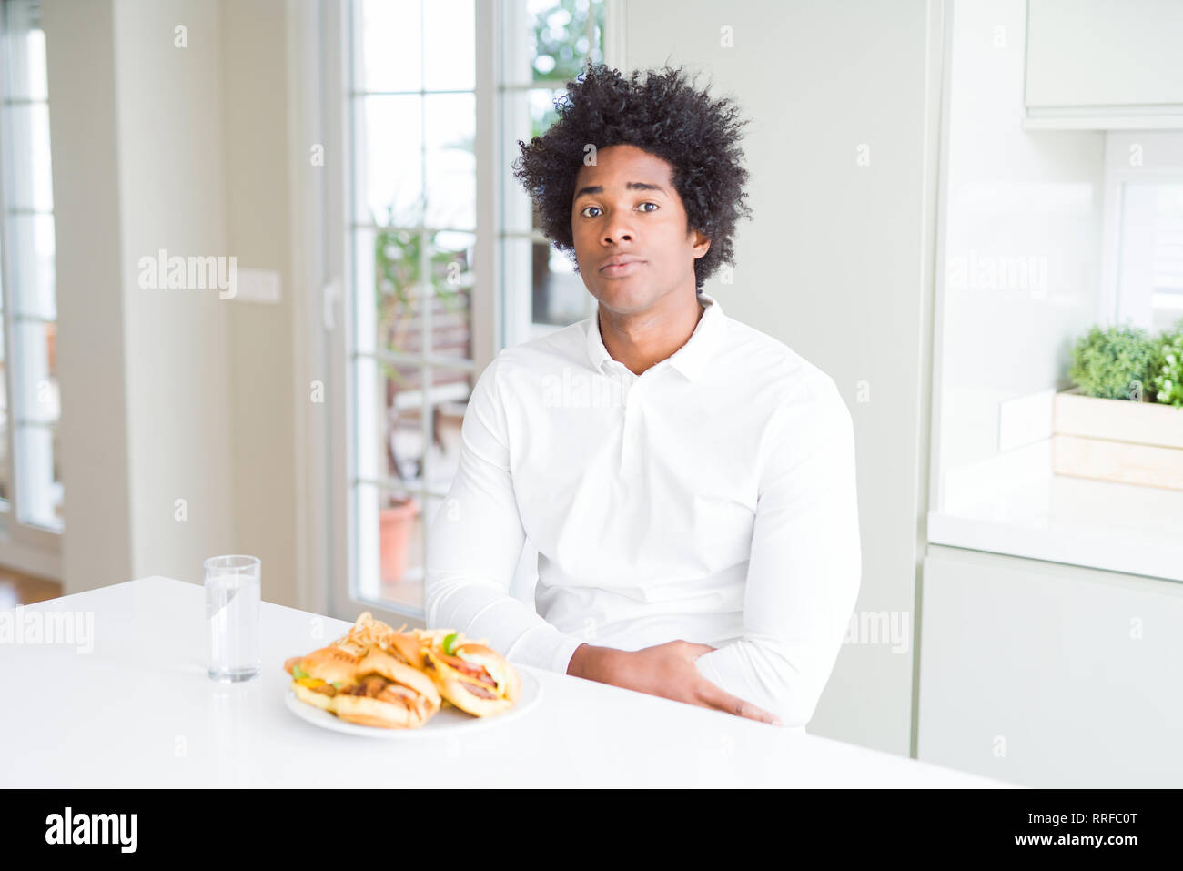 African American hungry man eating hamburger for lunch with serious ...