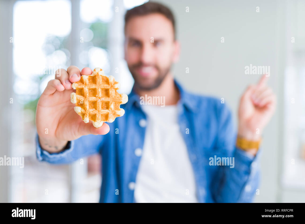 Handsome man eating sweet Belgian pancakes very happy pointing with ...