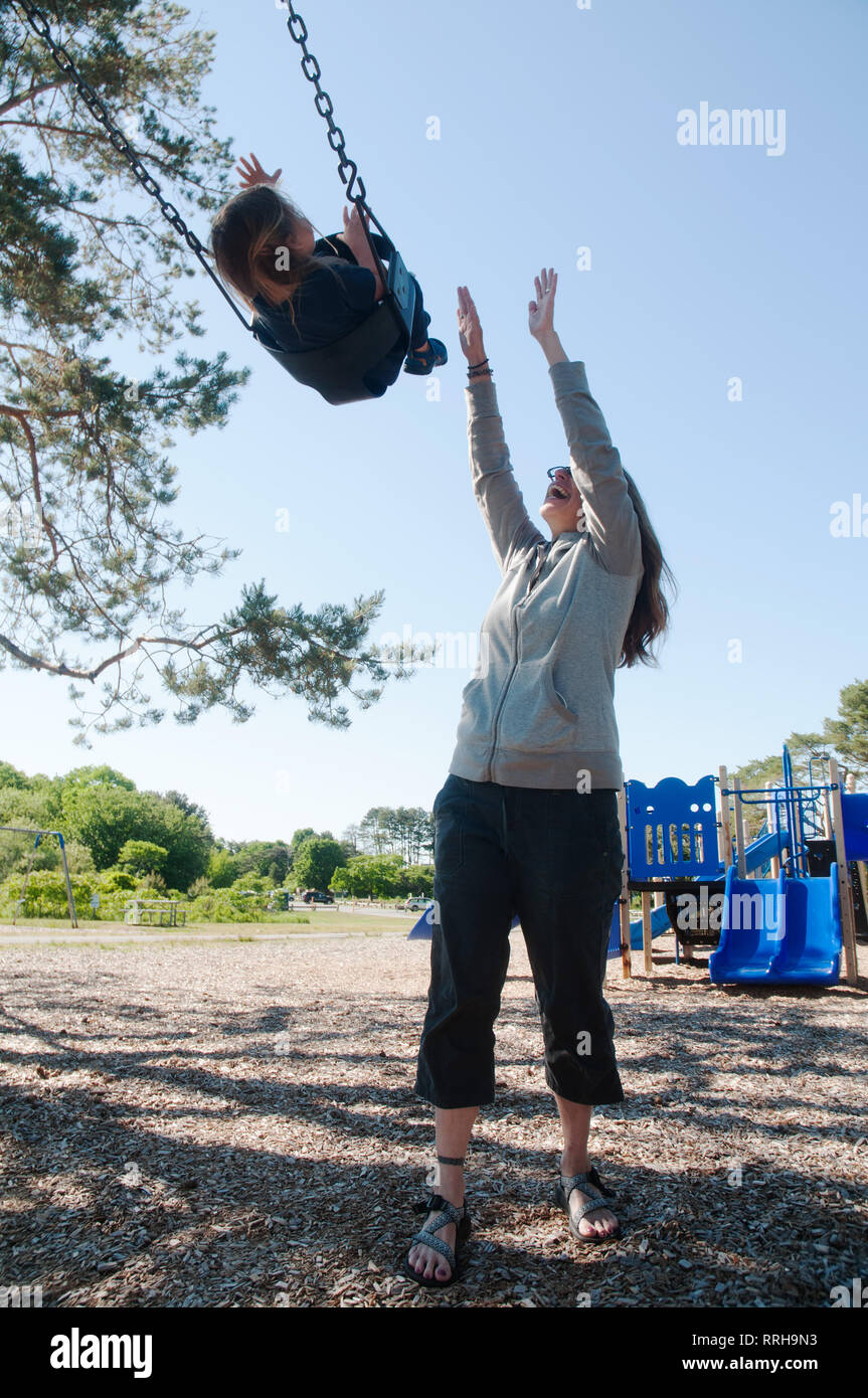 Smiling Mid-Adult Woman Pushing Child in Playground Chair Swing Stock ...