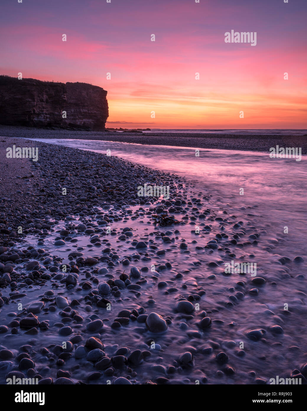The River Otter meets the sea with strong dawn colour, wet pebbles and ...