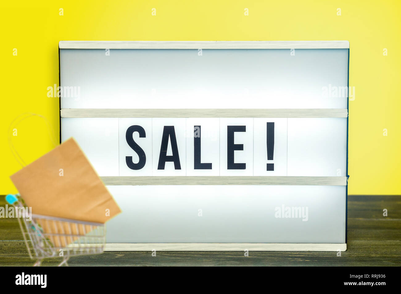 Light box with Sale letters and small shopping cart against yellow ...