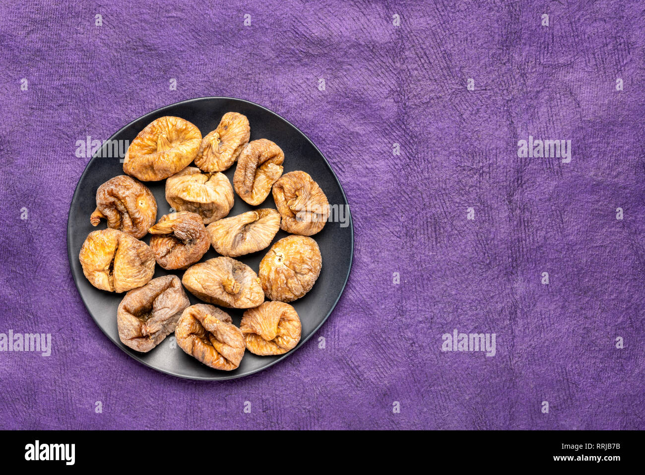 dried Turkish figs on a black plate against textured bark paper with a ...