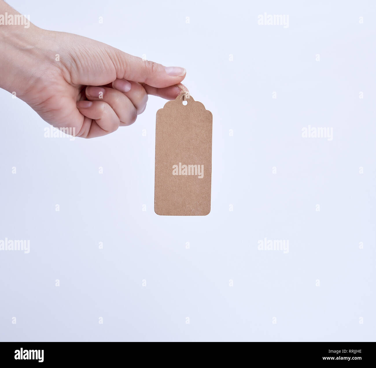 female hand holding a paper brown blank tag on a rope, white background ...