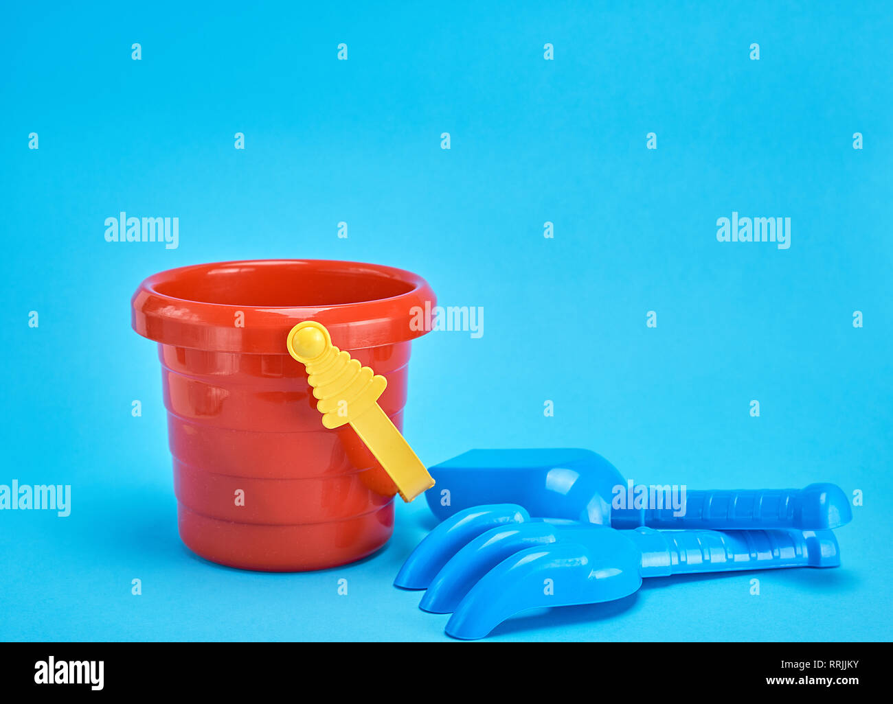 empty baby plastic red bucket and shovel with a rake on a blue ...
