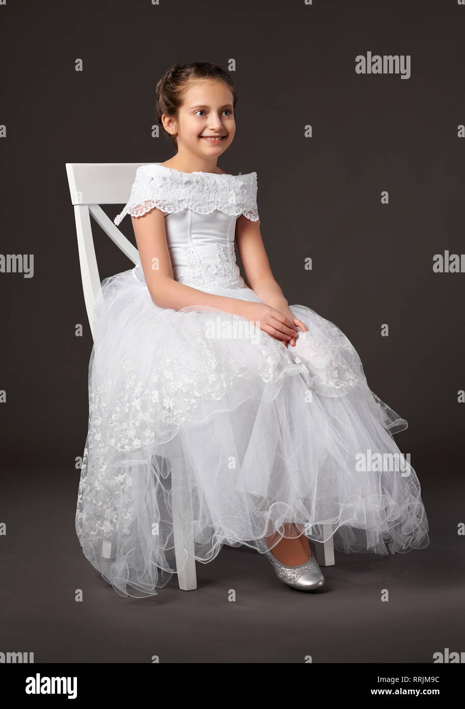 little girl dressed in a white ball gown and sitting on the chair, dark background Stock Photo ...