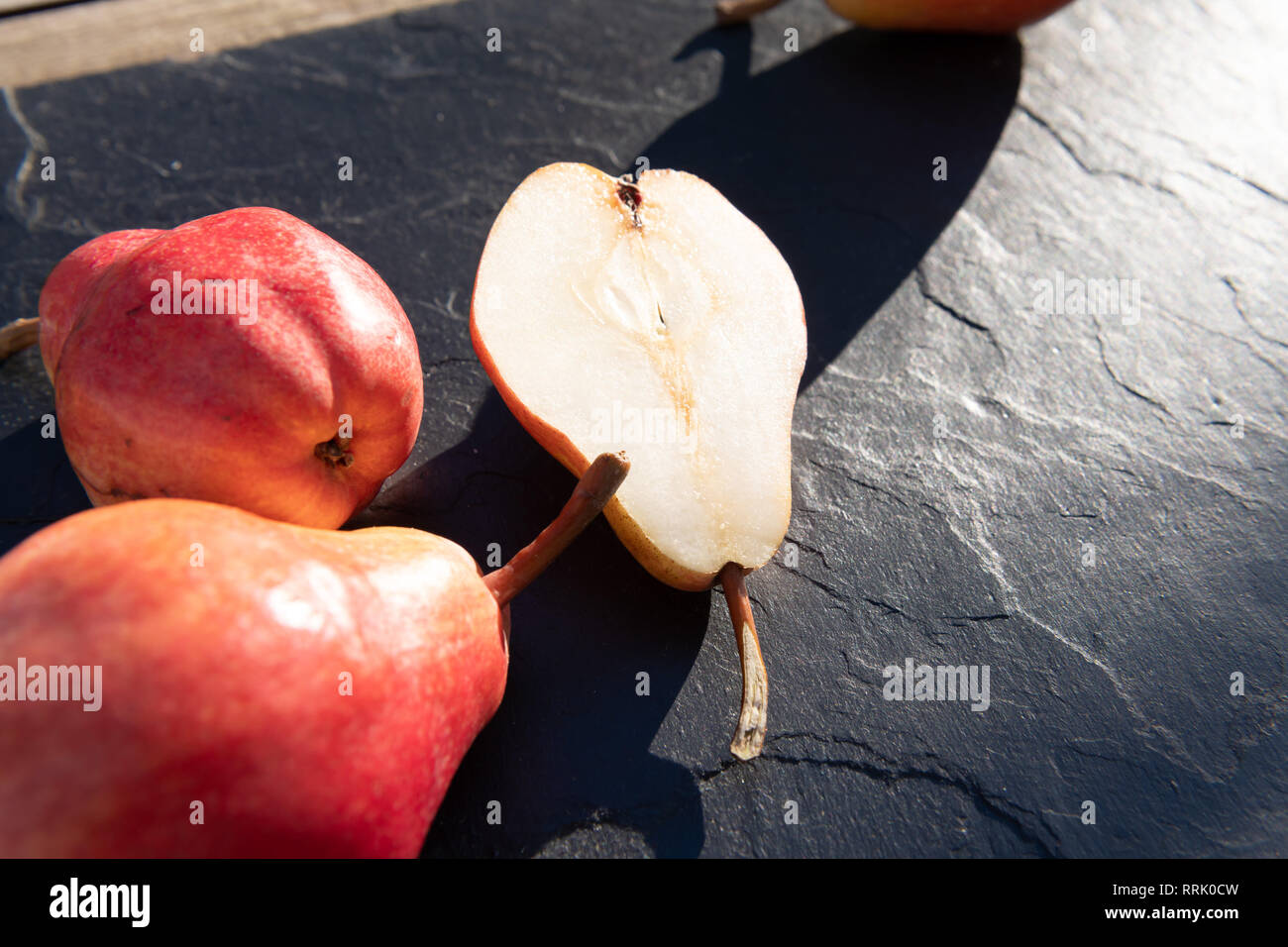 Cut red pears on slate board in sunlight ready to enjoy Stock Photo - Alamy