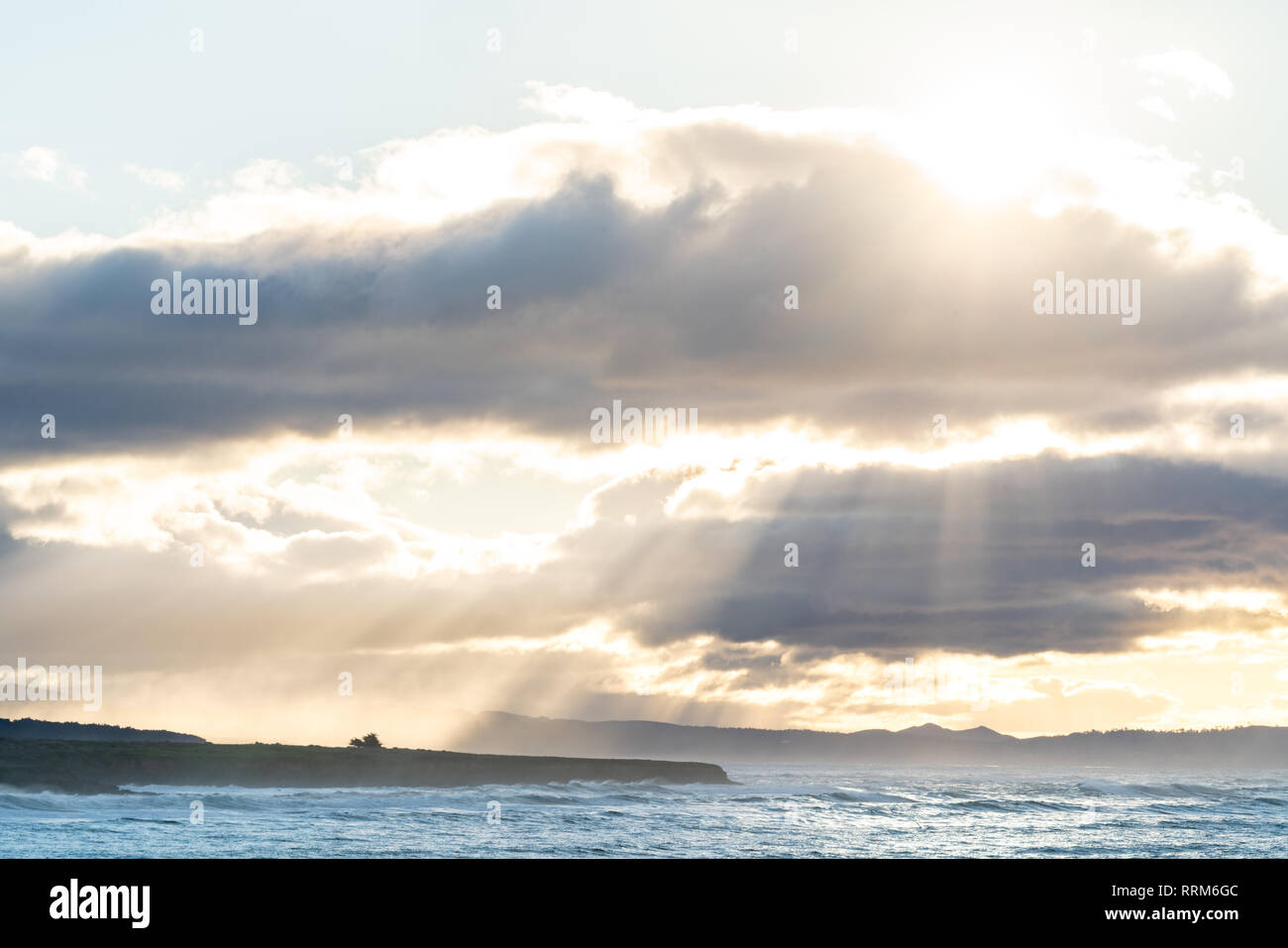 Sun light streams through parting clouds over the California coastline ...