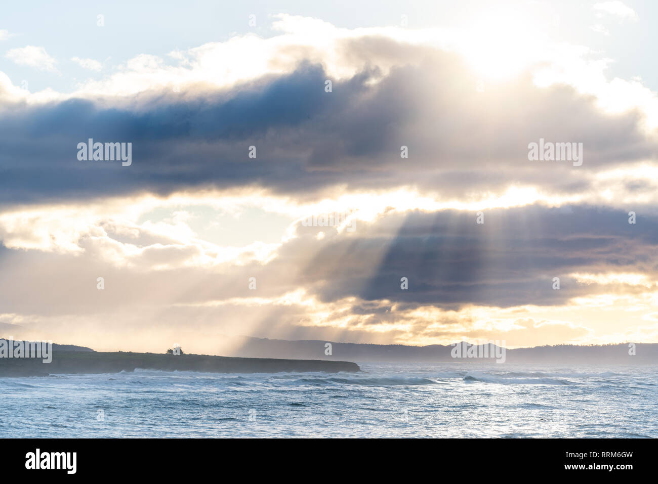 Sun light streams through parting clouds over the California coastline ...