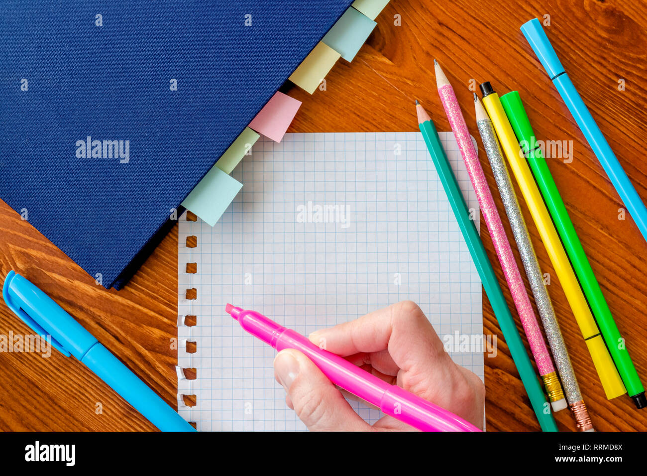 Hand holding pink highlighter, next to notebook with marked pages ...