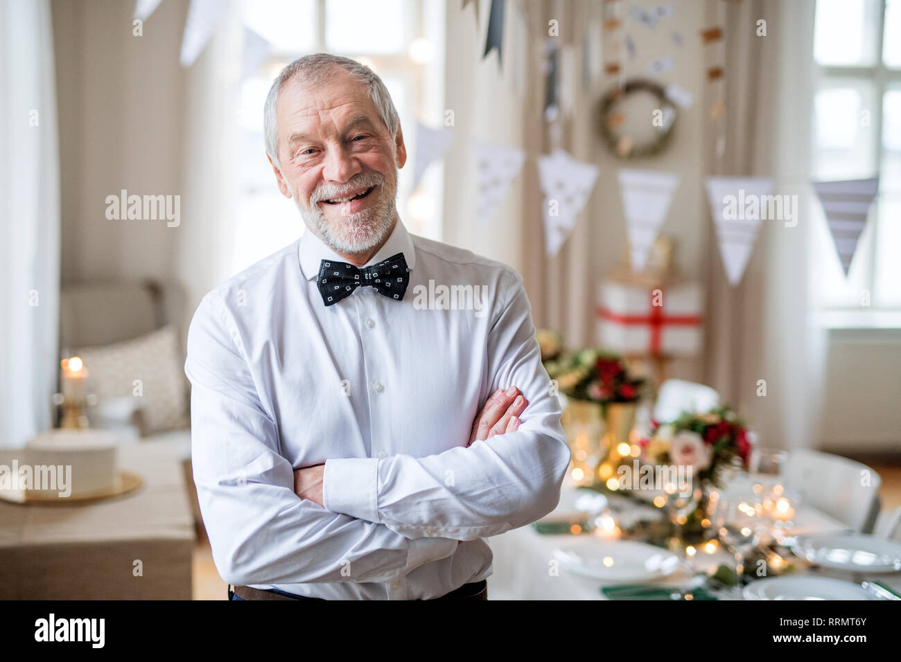 A portrait of a senior man standing indoors in a room set for a party ...
