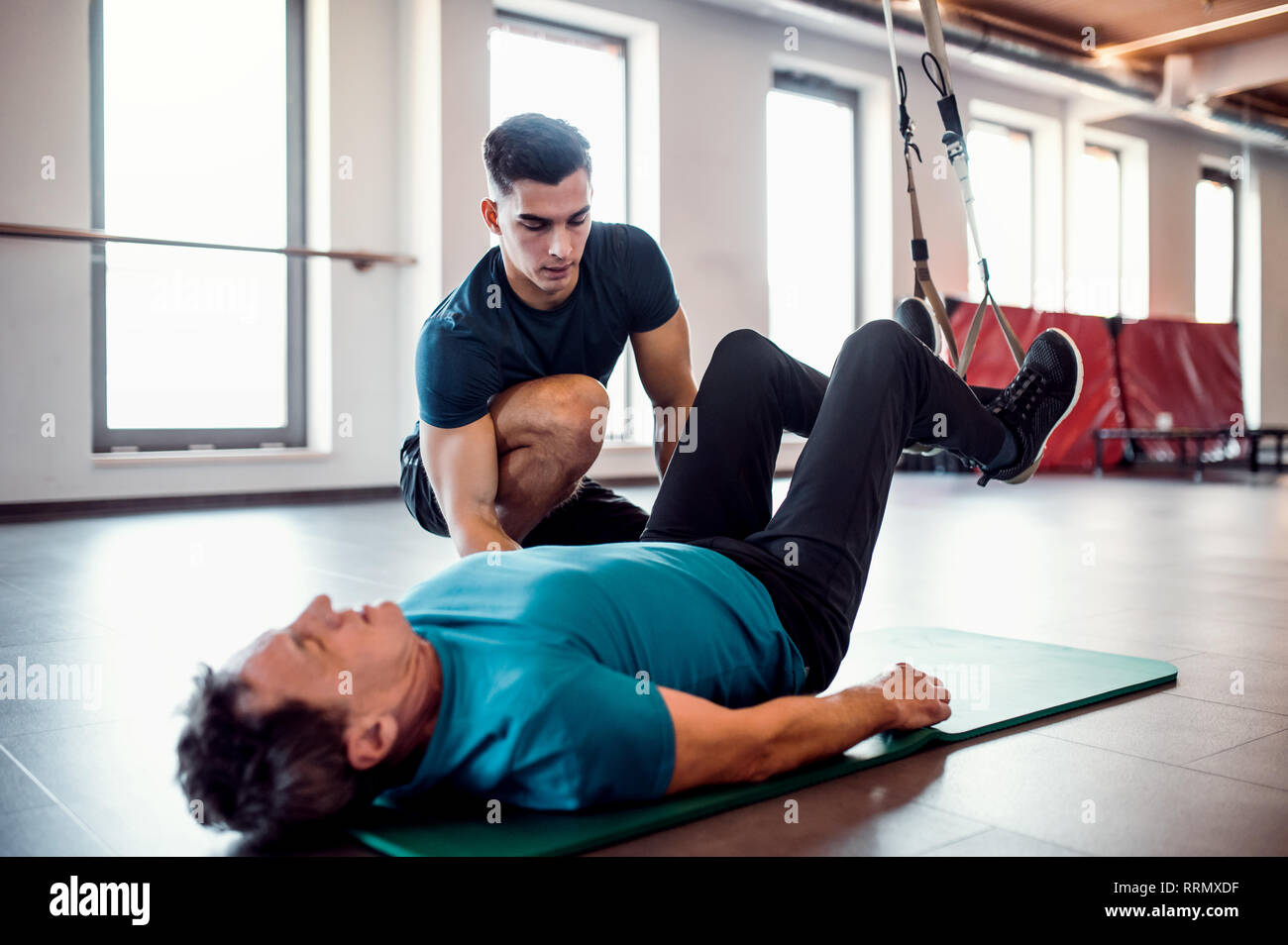 A senior man in gym and a handsome personal trainer doing exercise with ...