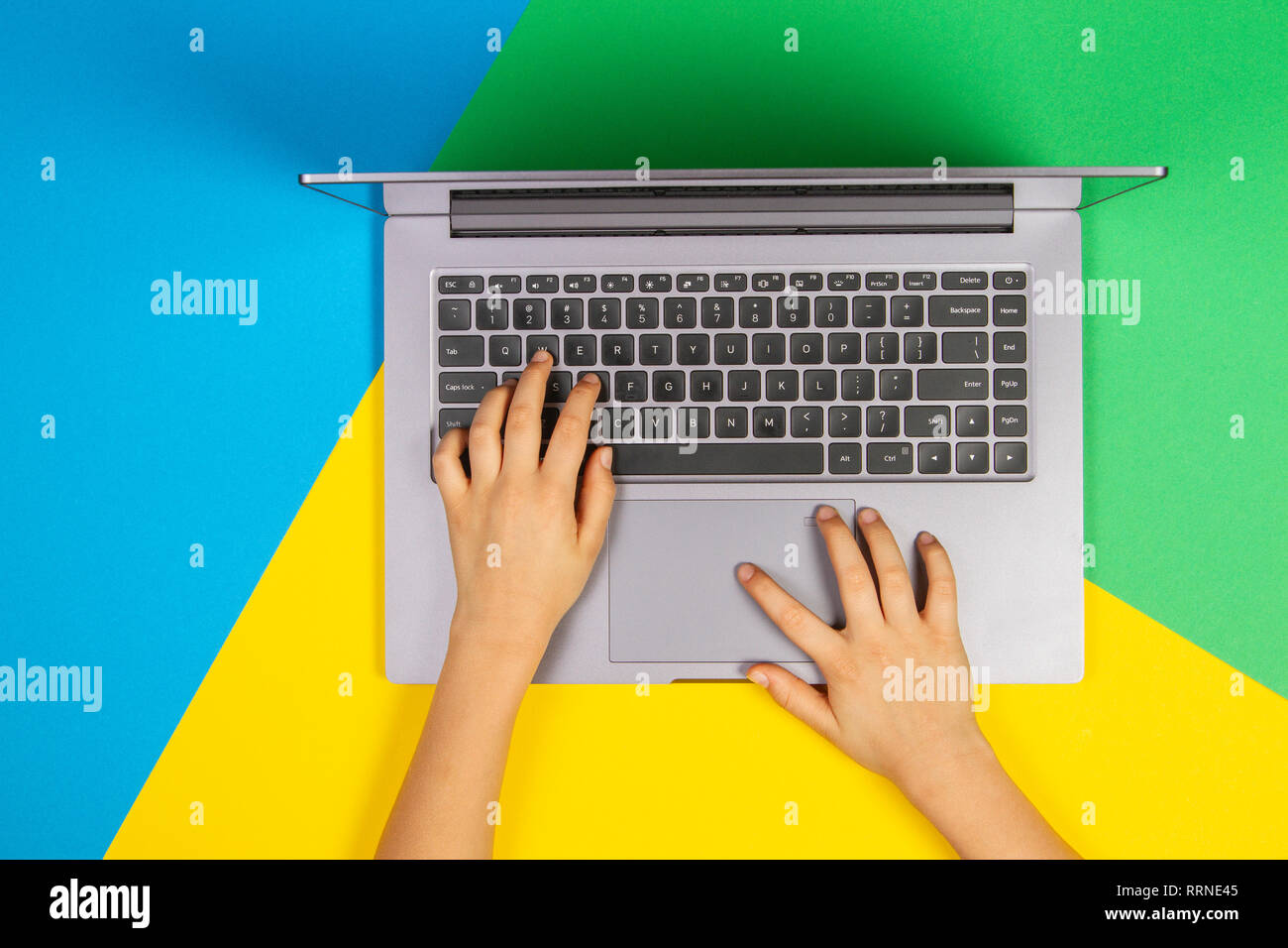 Kid hands typing on laptop computer keyboard on multicolored background ...