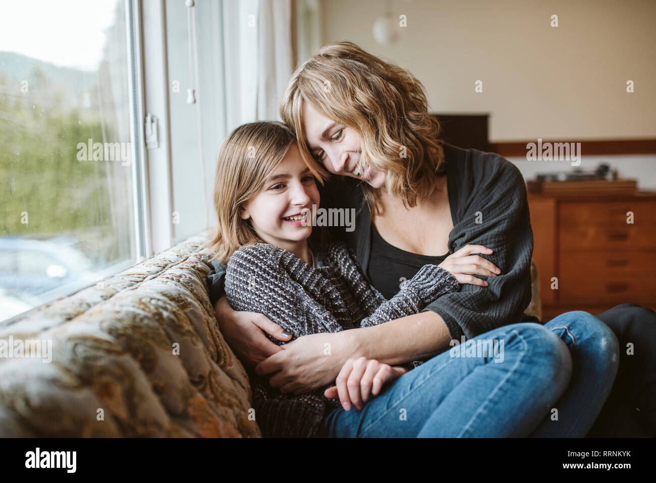Affectionate Mother And Daughter Cuddling On Living Room Sofa Stock