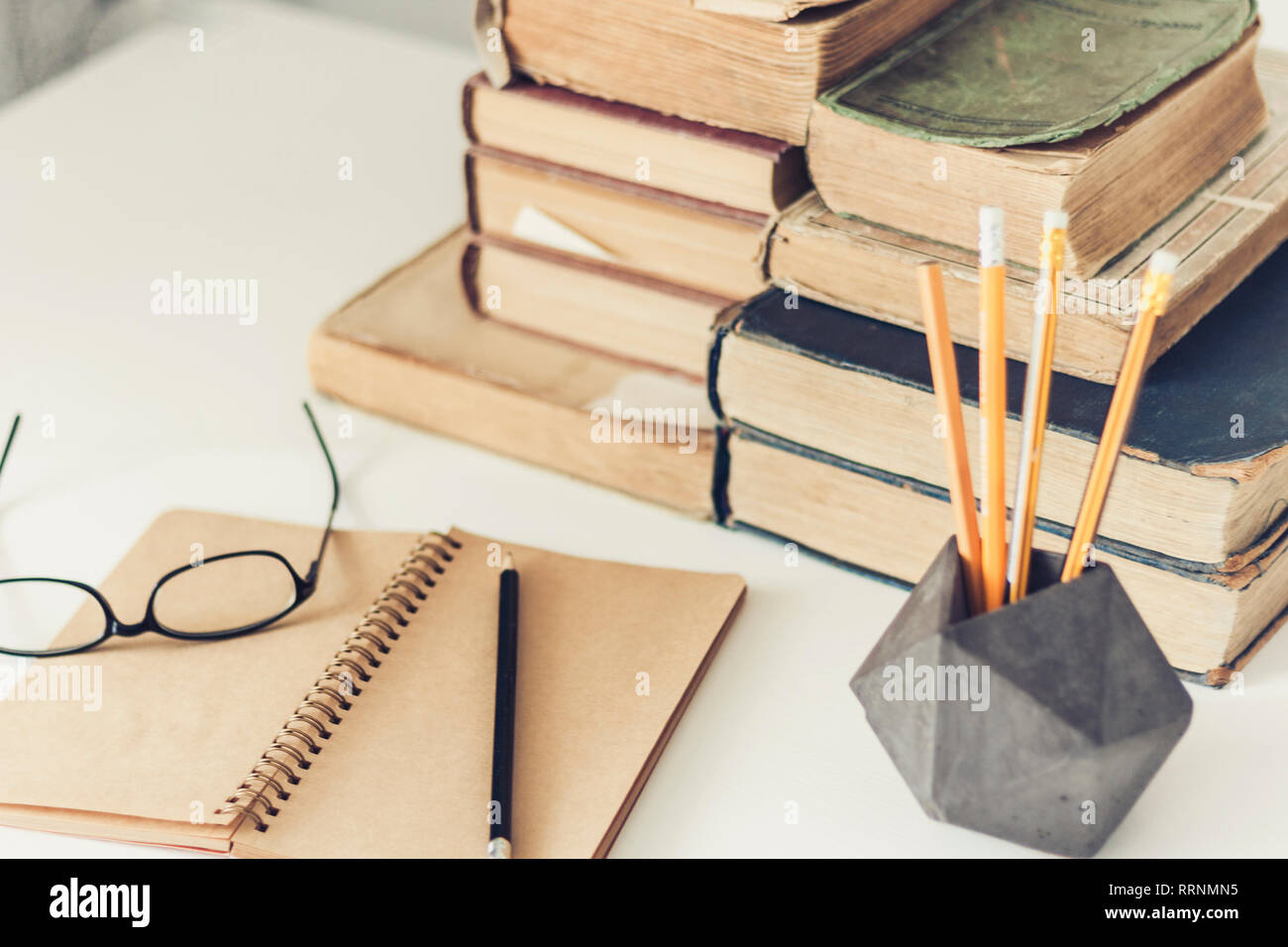 Stack of old books, textbook, glasses and pencils in office background ...