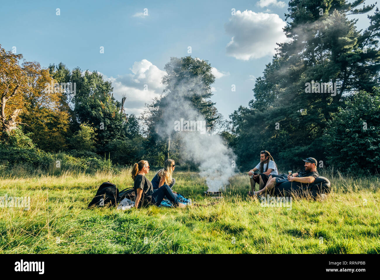 Friends camping, relaxing around campfire in remote field Stock Photo ...