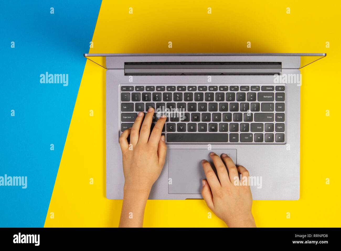Kid hands typing on laptop computer keyboard, top view, yellow and blue ...