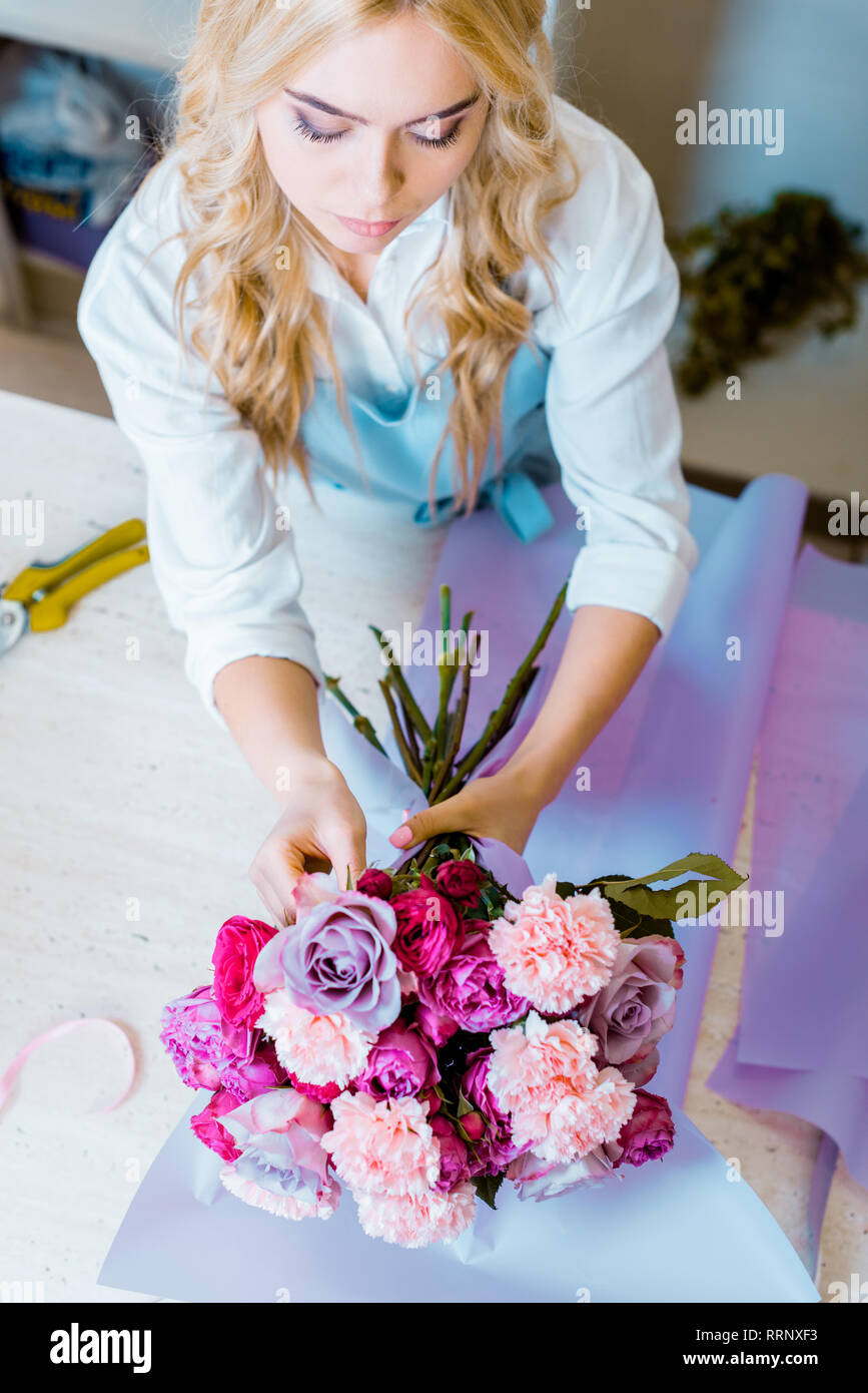 beautiful female florist arranging bouquet with roses and carnations in ...