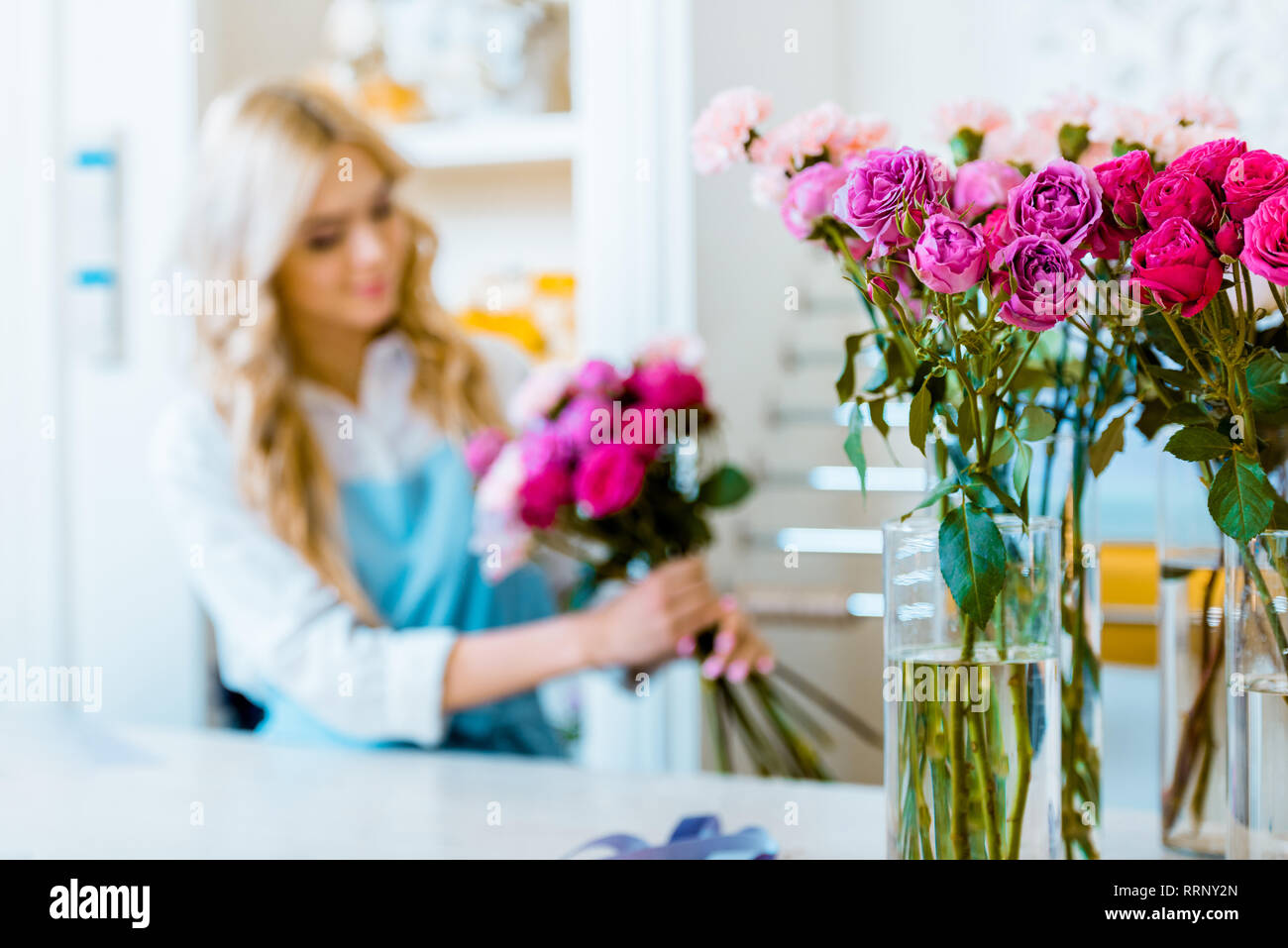 selective focus of roses with female florist arranging bouquet in ...