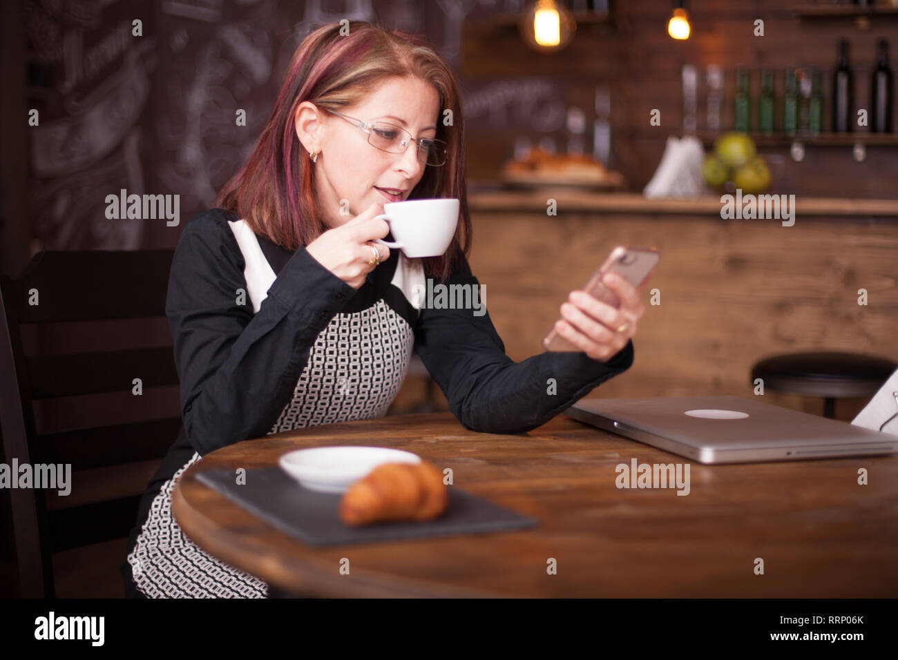 Adult businesswoman reading emails from her phone while having a cup of ...