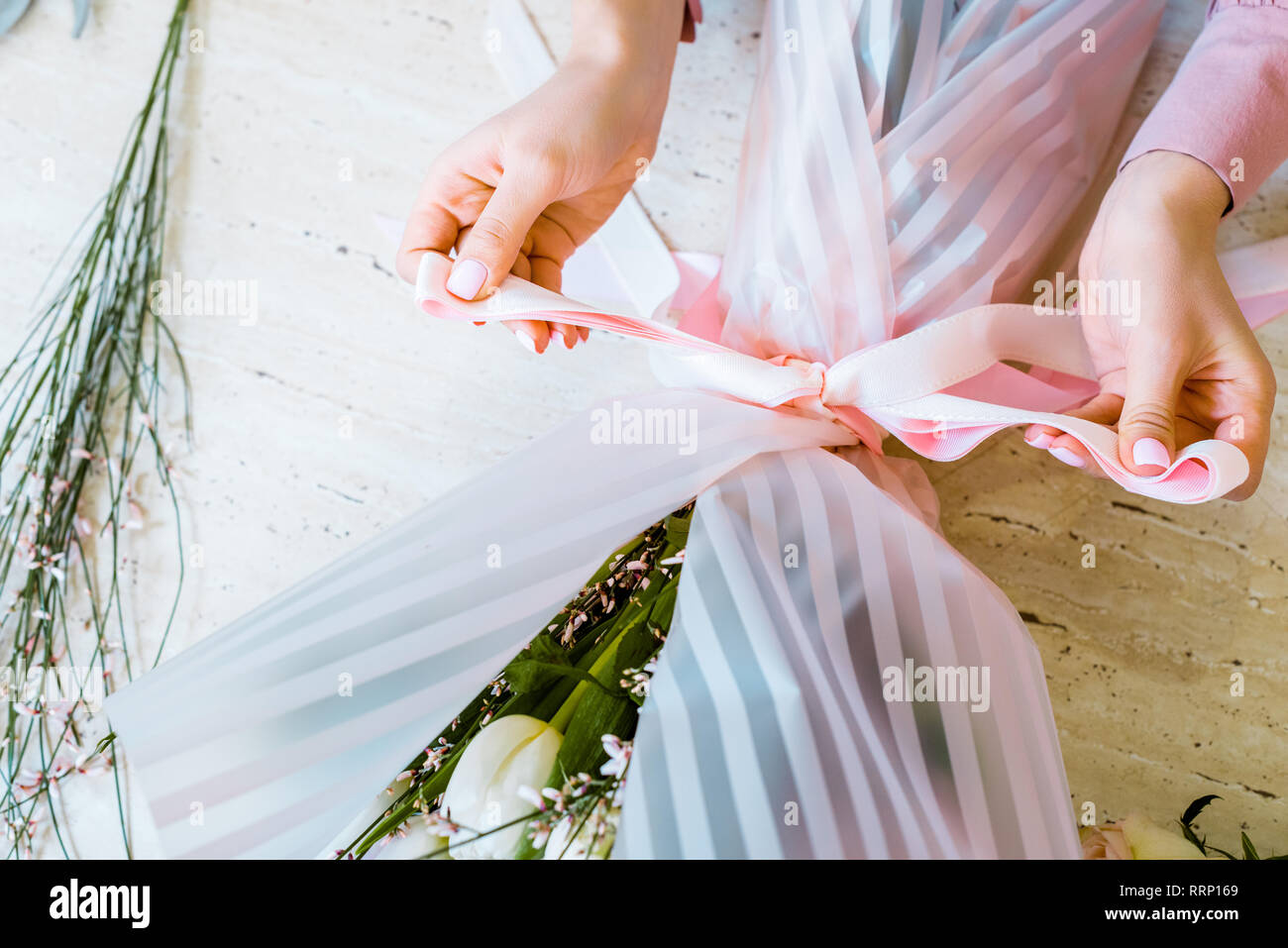 partial view of female florist tying bow with ribbon while wrapping ...