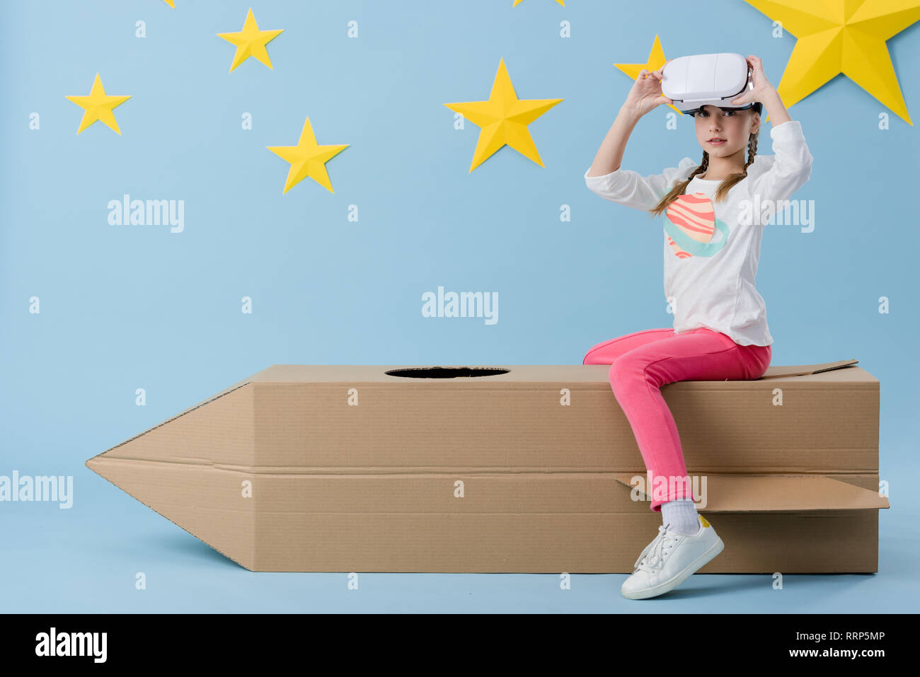 Kid sitting on cardboard rocket and taking off vr headset on blue ...