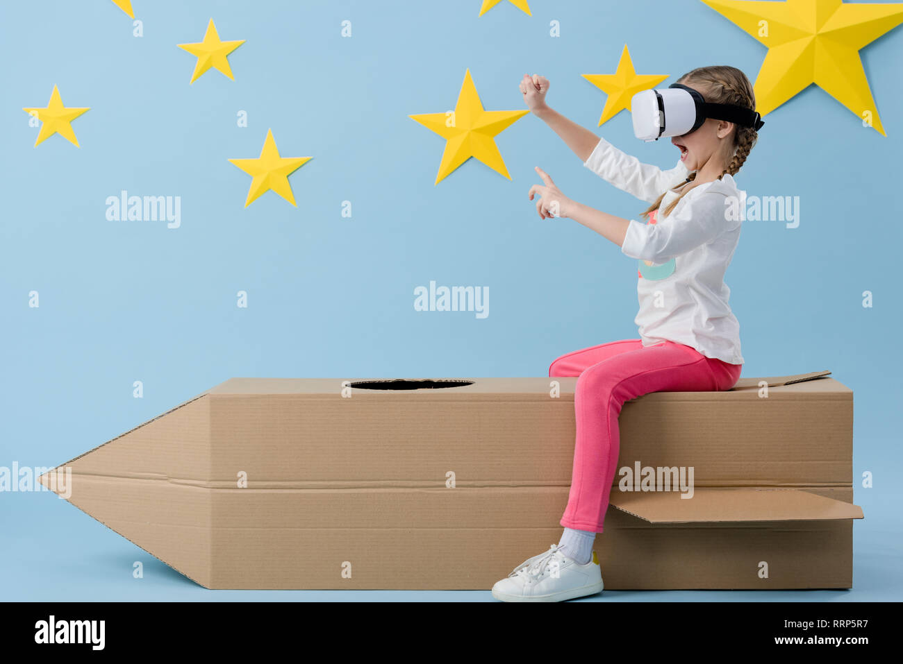 Child in vr headset sitting on cardboard rocket and waving hands on ...