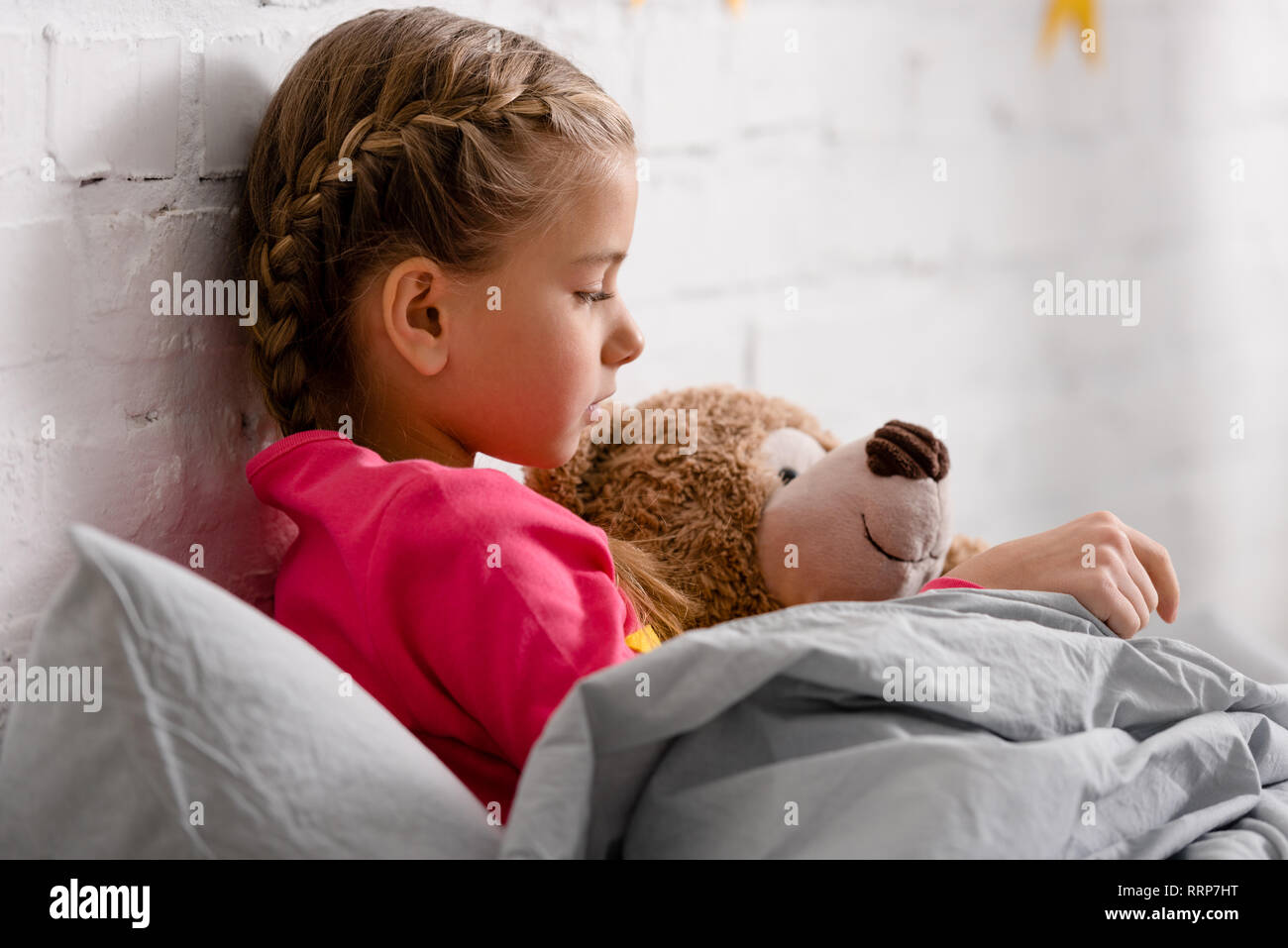 Side view of cute child lying in bed with teddy bear Stock Photo - Alamy