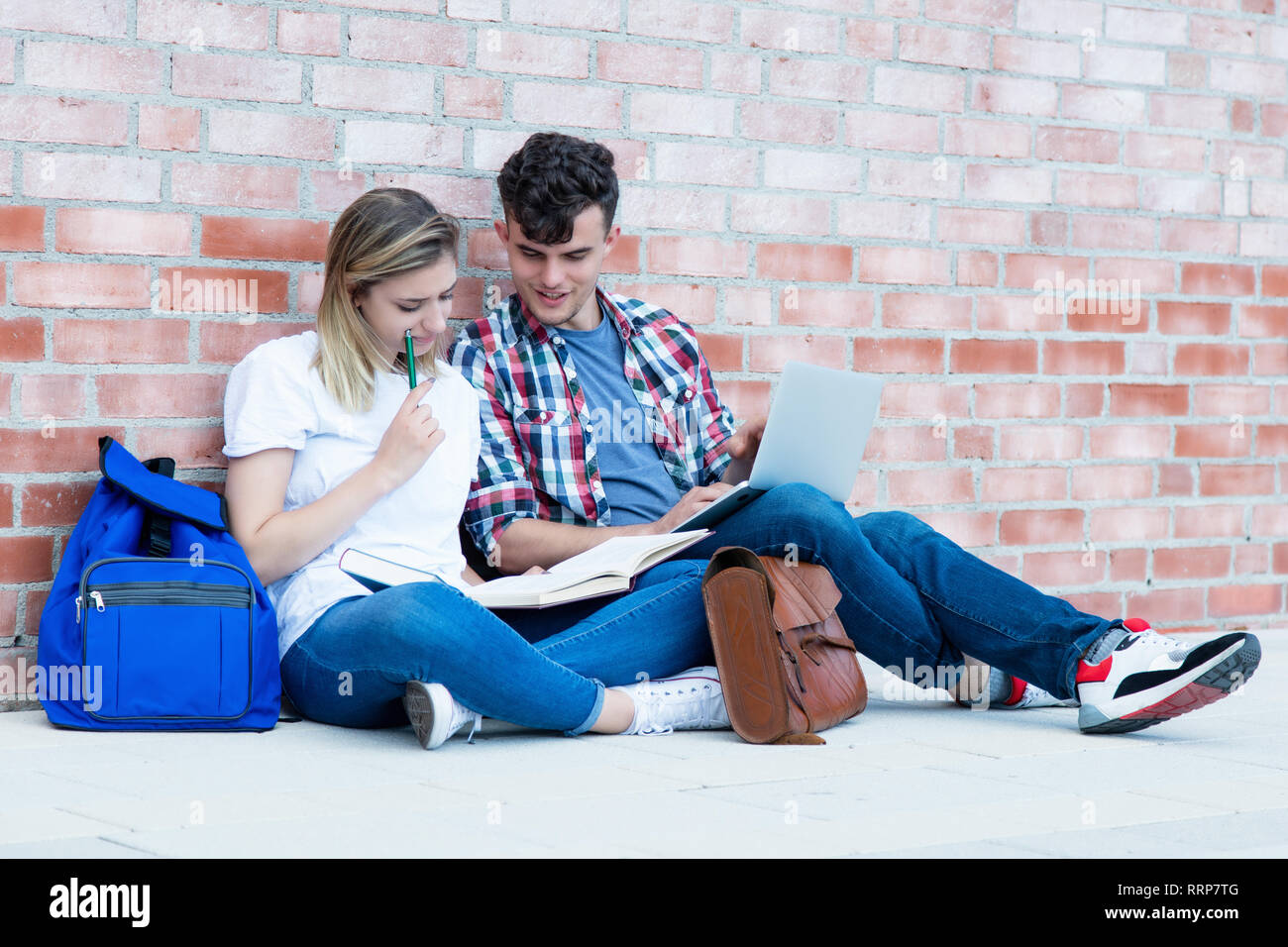 Two learning german students with book and laptop outdoor on campus of ...