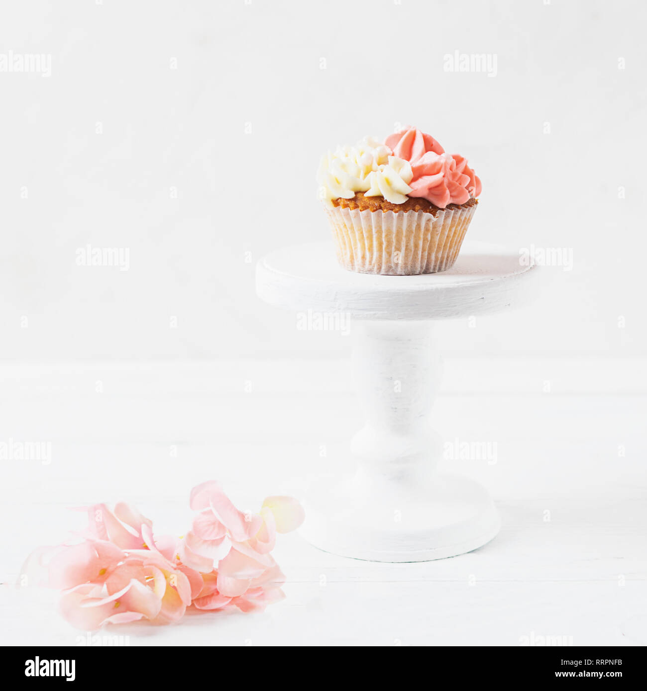 Muffin is decorated with thick white and pink cream on a light ...