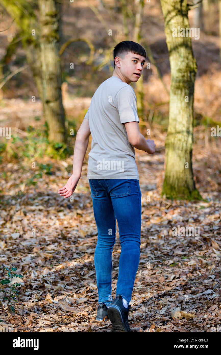 Teenage caucasian boy walking away through woodland on a warm spring ...