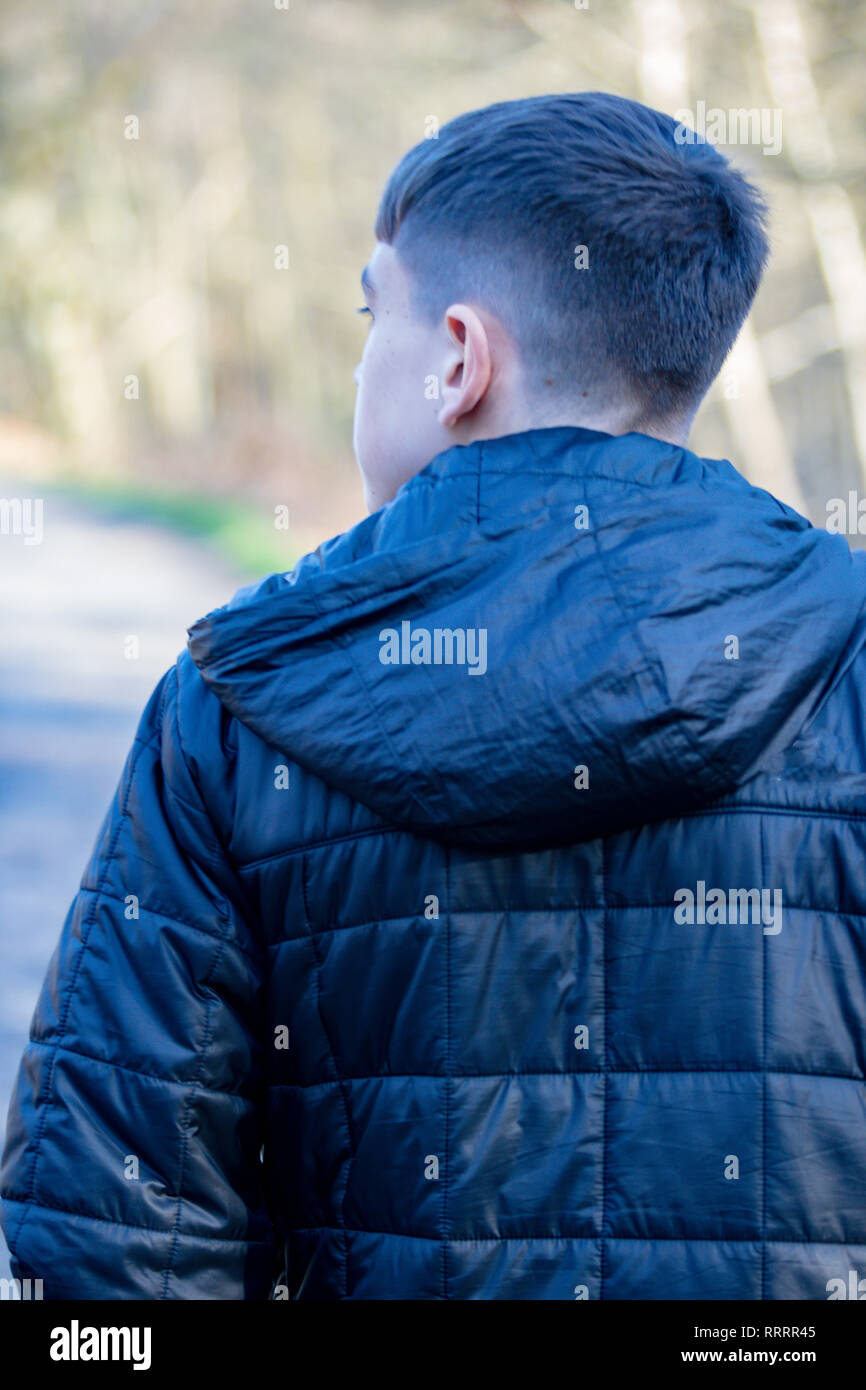 Caucasian teenage boy walking away wearing a jacket on a spring day ...