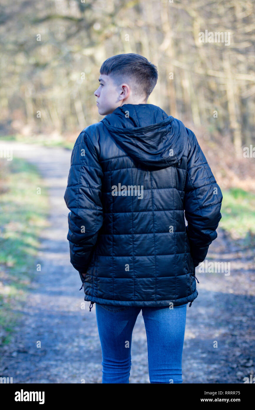 Caucasian teenage boy walking away wearing a jacket on a spring day ...