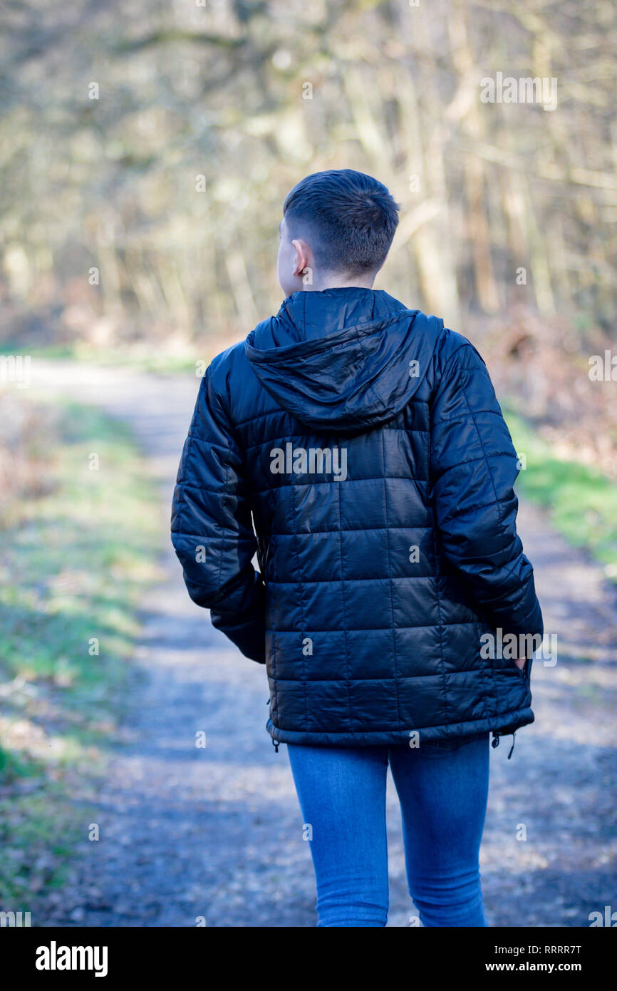 Caucasian teenage boy walking away wearing a jacket on a spring day ...