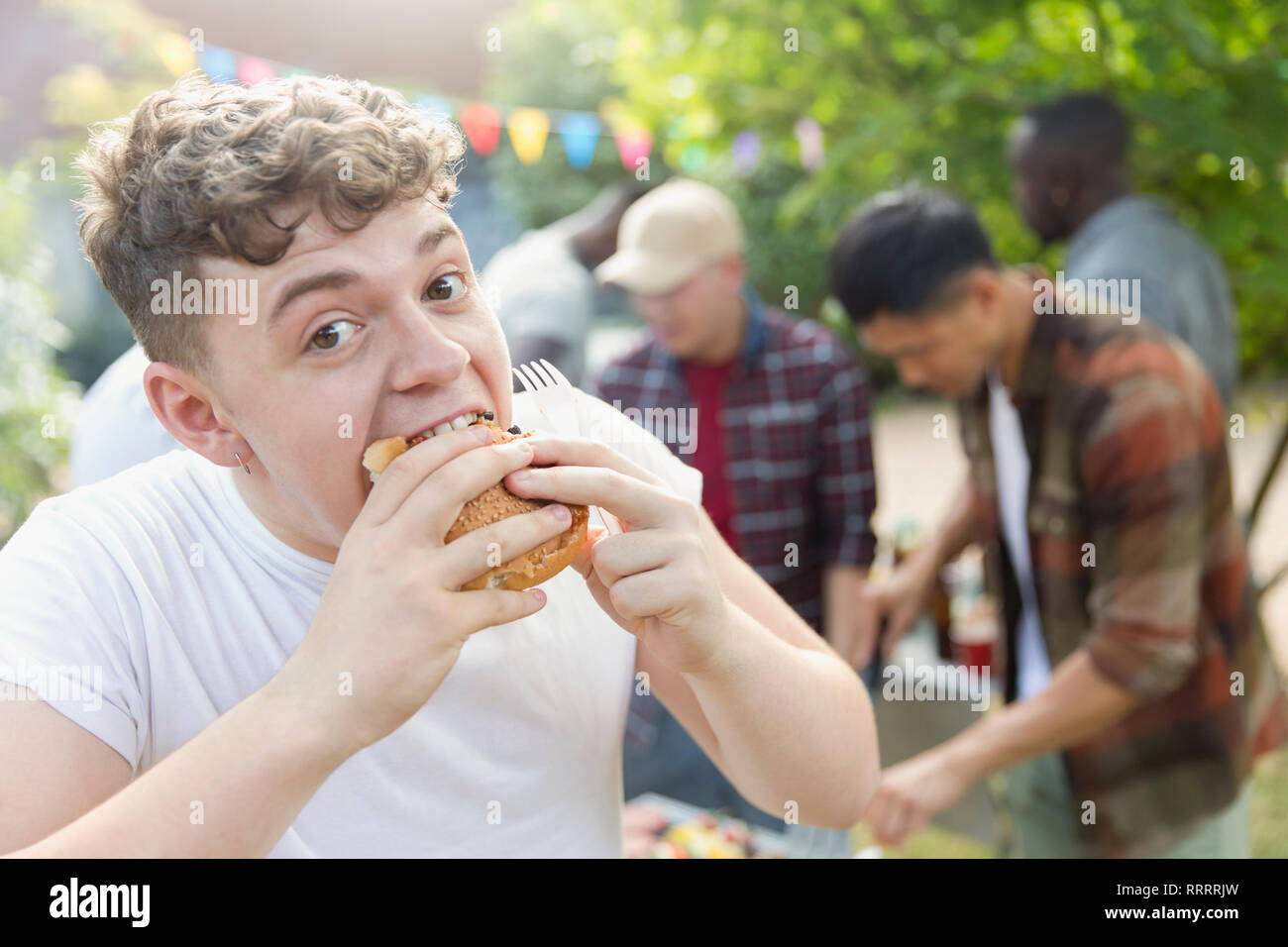 Portrait hungry teenage boy eating hamburger at backyard barbecue Stock ...