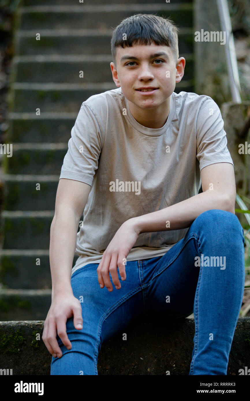 Portrait of a caucasian teenage boy sitting outside on concrete steps ...