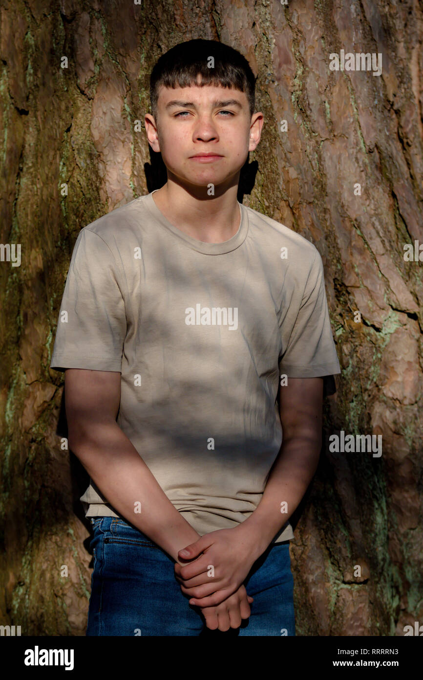 Portrait of a caucasian teenage boy leaning against a tree on a warm ...