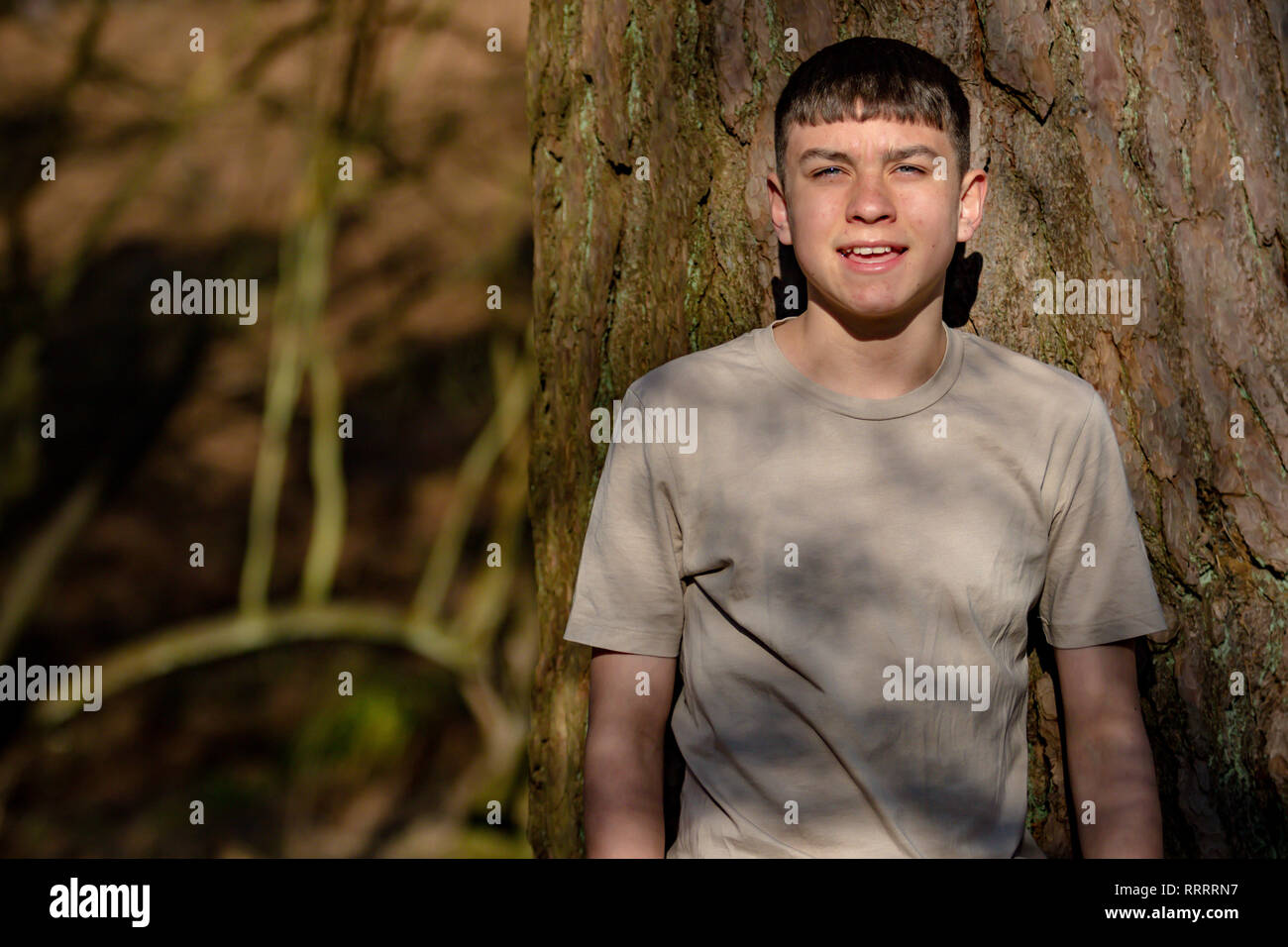 Portrait of a caucasian teenage boy leaning against a tree on a warm ...